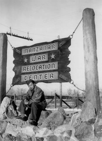 Pvt. Ben Hatanaka seated under Manzanar War Relocation Center sign ...