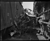 Mangled remains of an automobile lie between 2 train cars, [between ...