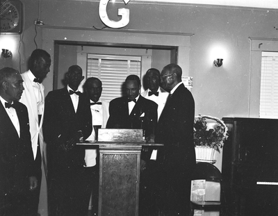 Seven men standing at podium in masonic meeting room — Calisphere