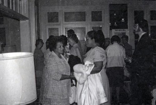Two women talking in a crowded room — Calisphere