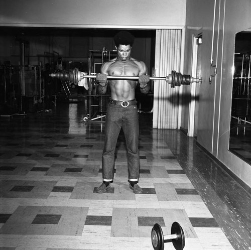 Man lifting weights in the Compton College gym, Compton, 1972 — Calisphere