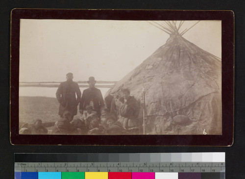 Two Caucasian men with Alaskan natives outside native house — Calisphere