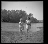 Frances and Elizabeth West stand in water by the muddy shore, Anaheim ...