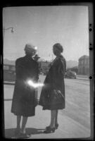 Mertie West and a fellow ship passenger stand and chat on a sidewalk ...