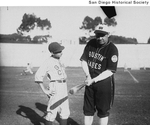 Babe Ruth holding a baseball bat as a boy in a baseball uniform looks ...