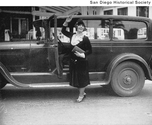Aimee Semple McPherson waving as she stands next to the open door of an ...