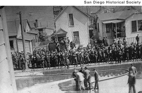 A crowd watches a group of men operate a fire hose during the 1912 I.W ...
