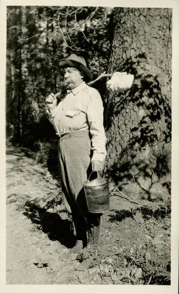 Woman holding a bucket and bindle with a cigar in her mouth beside a ...