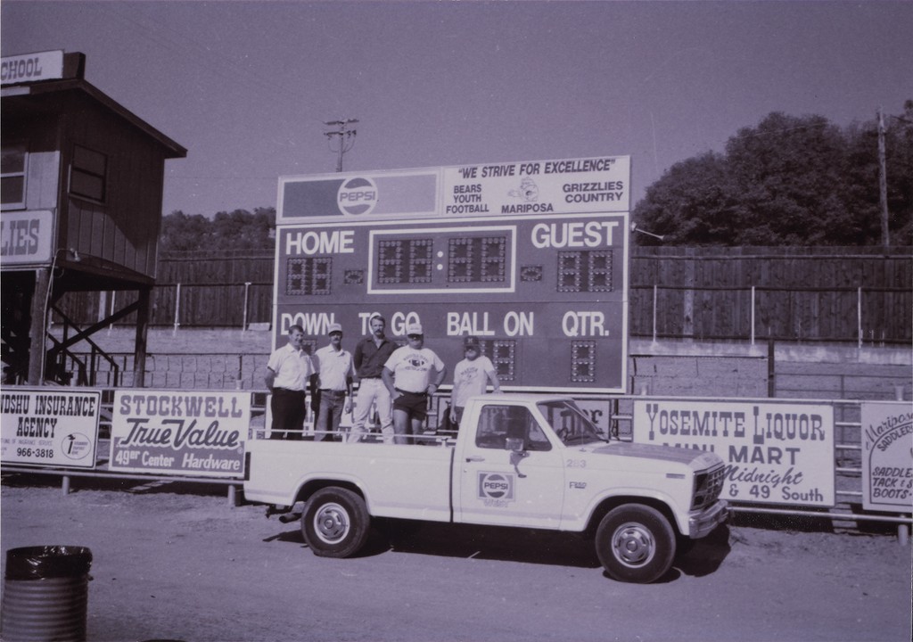[Men stand on truck trunk at football field] — Calisphere